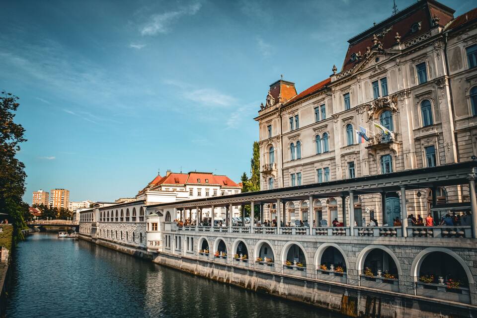 Uma ponte de pedra com arcos sobre um rio, ladeada por edifícios históricos com telhados vermelhos e varandas.