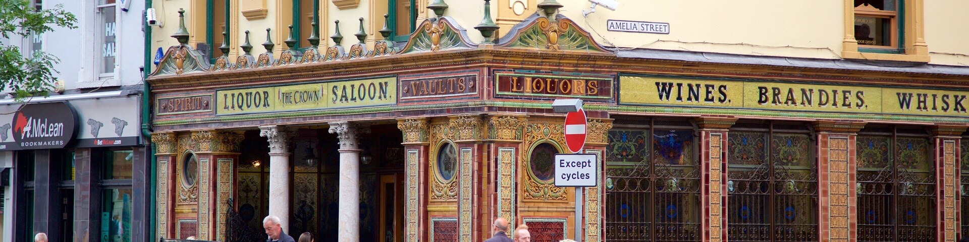 Um edifício histórico com arquitetura ornamentada, incluindo colunas e molduras decorativas. A fachada exibe placas com os dizeres 'Spirits', 'Liquor', 'The Crown', 'Saloons', 'Vaults', 'Liquor', 'Wines', 'Brandy' e 'Whiskey'.