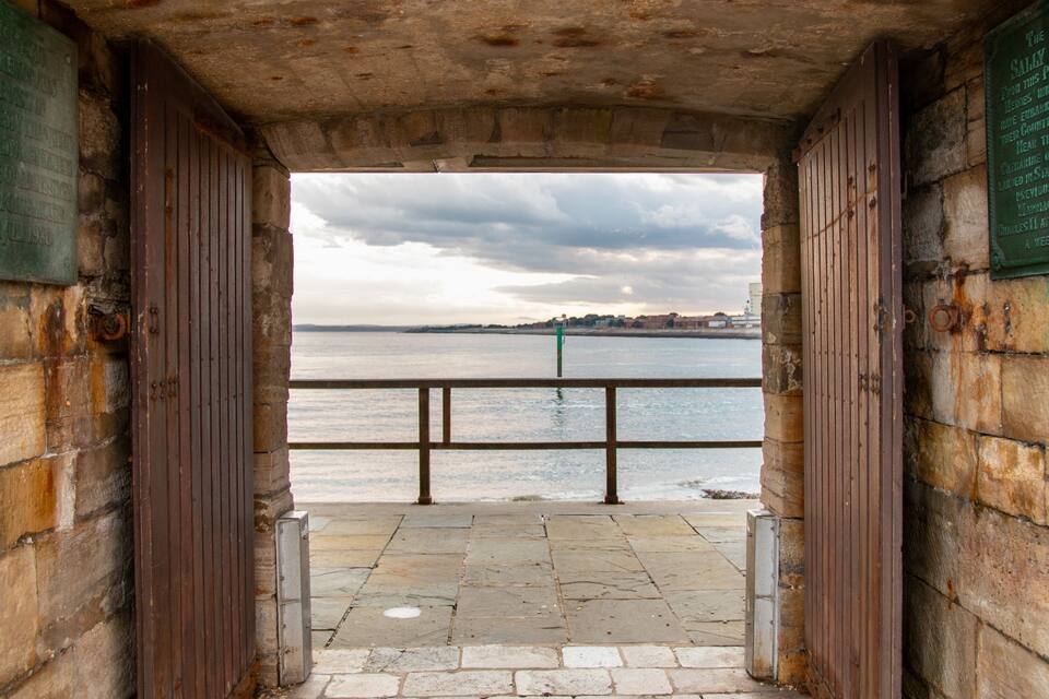 Um arco de pedra que dá acesso a uma vista para a água.