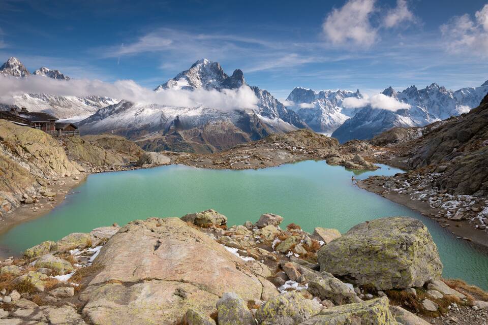 Um lago montanhoso rodeado por terreno acidentado e picos nevados.