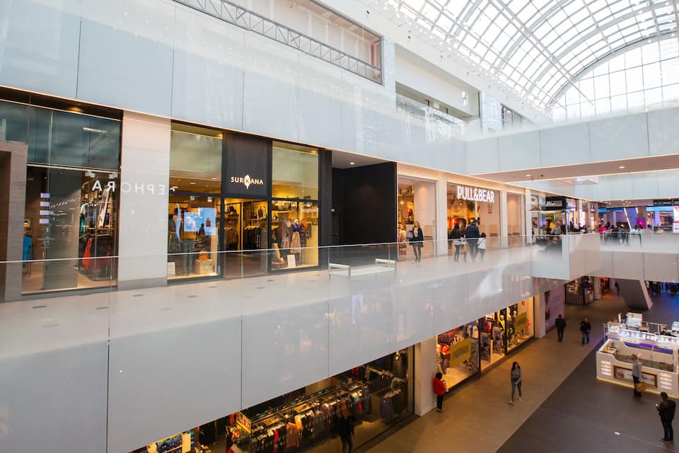 Um centro comercial com vários andares e diversas lojas, incluindo uma loja de roupas chamada SUREKANS e outra chamada PULL&BEAR.