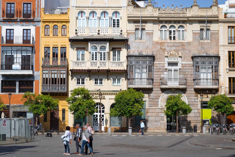Ruas com edifícios históricos, um banco e algumas pessoas caminhando.
