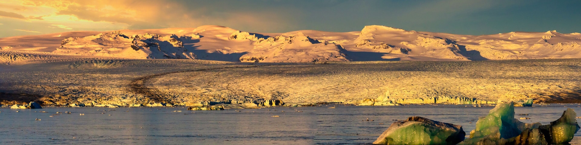 Um glaciar com icebergs em um corpo d'água, montanhas ao fundo e um céu nublado.