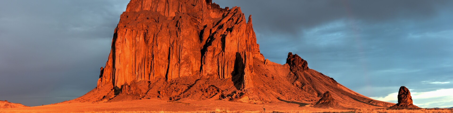 Paisagem montanhosa acidentada com uma formação rochosa imponente e uma trilha de terra que a leva.