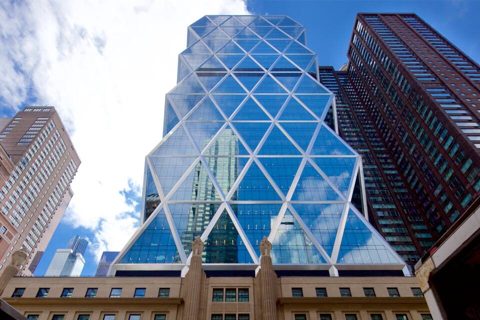 Um arranha-céu moderno de vidro com design triangular, rodeado por outros edifícios altos.