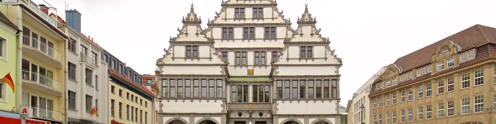 Um edifício histórico com arquitetura elaborada, uma fonte central e lojas e cafés ao redor.