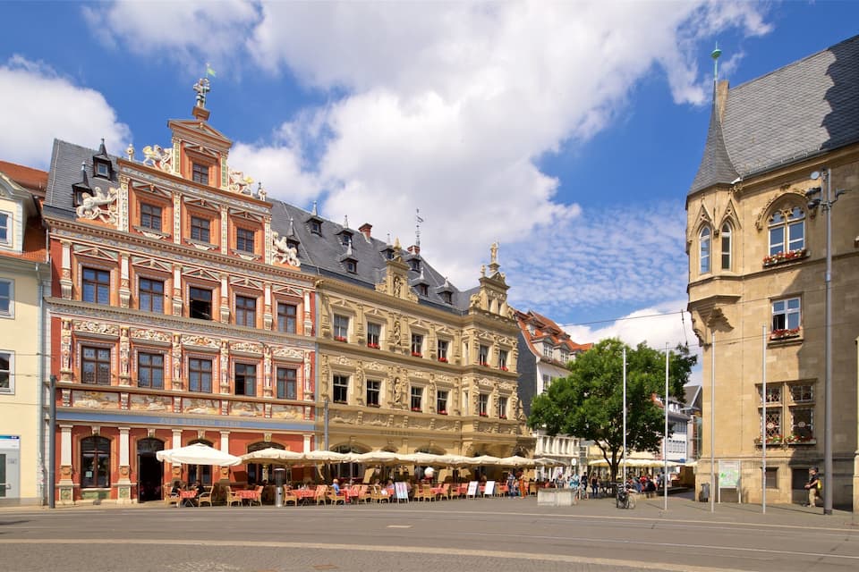 Uma rua histórica europeia com edifícios ricamente decorados, cafés ao ar livre e um céu azul límpido.