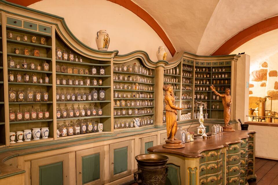 Uma farmácia antiga com prateleiras cheias de garrafas de vidro e recipientes de cerâmica.