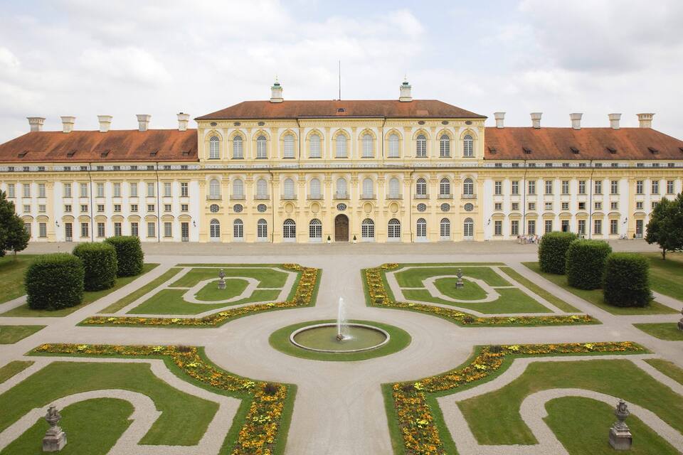 Um amplo edifício clássico com jardins simétricos e uma fonte central.
