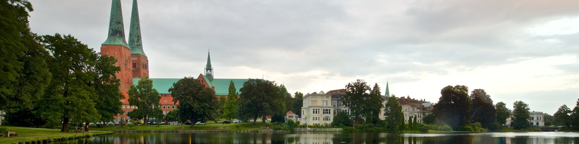 Um lago tranquilo reflete uma igreja com duas torres e vegetação ao redor.