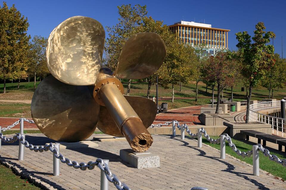 Um grande canhão de bronze em um parque, com um edifício ao fundo.
