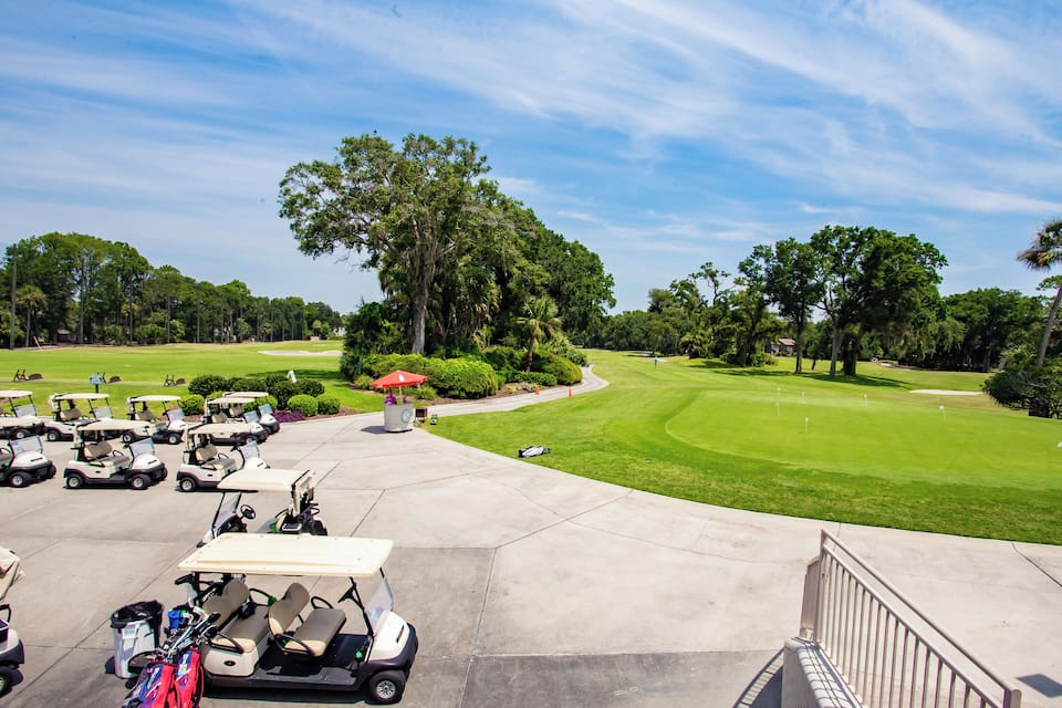 Um campo de golfe com vários carrinhos de golfe estacionados perto de um clube.