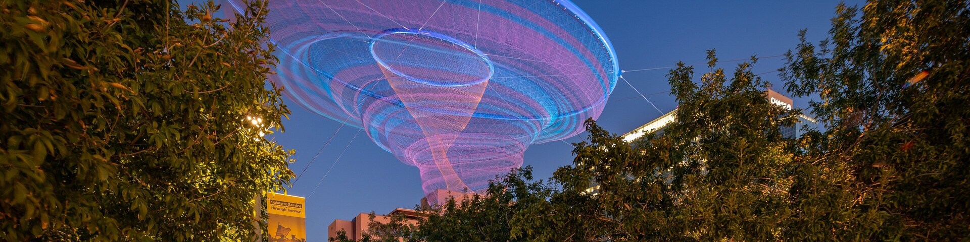 Uma estrutura grande e iluminada, parecida com um funil gigante, em um parque ao entardecer.