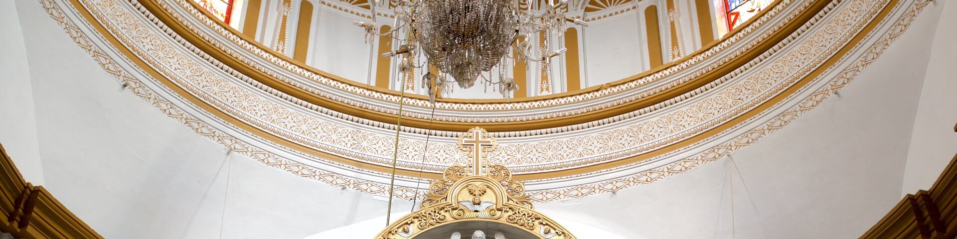 Interior ornamentado com um grande candelabro, decorações douradas e uma estátua central de um anjo segurando uma criança.