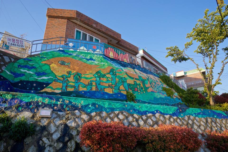 Um mural colorido numa parede de pedra, com um edifício ao fundo.