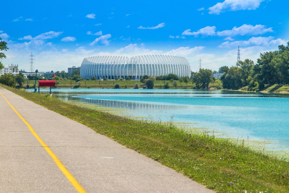 Um estádio com design único, um rio e um céu azul límpido.