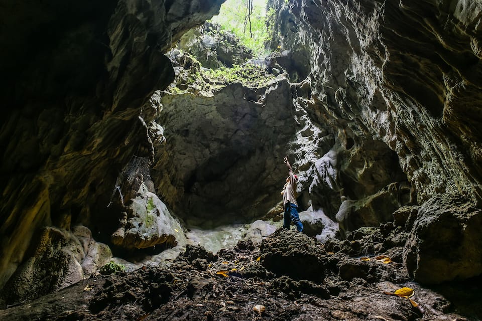Caverna com estalactites e estalagmites, uma pessoa em uma rocha e uma pequena piscina de água.
