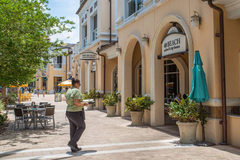 A street with outdoor seating, a man walking, and a building with a sign reading "400 BEACH seafood & tap house".