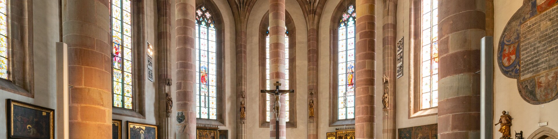 Interior de igreja com alta abóbada, janelas de vitrais e altar central.