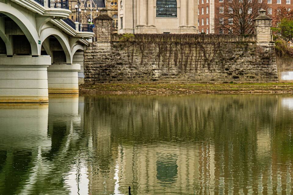 Um rio com uma ponte e uma estátua em um pedestal ao fundo.