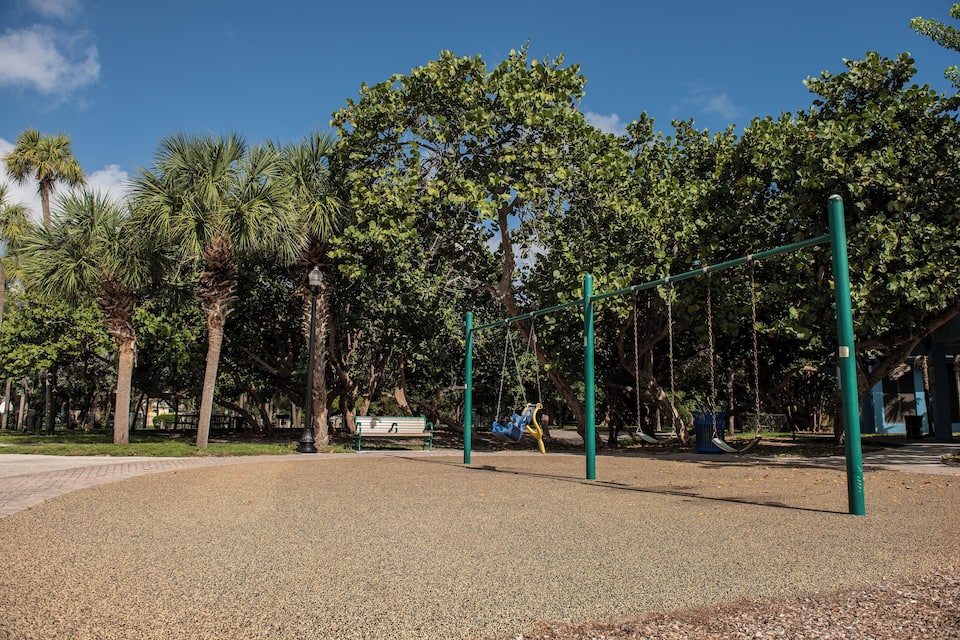 Parque com palmeiras, baloiços e um banco.