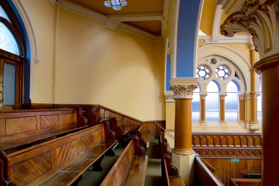 Interior com bancos de madeira, um relógio e vitrais.