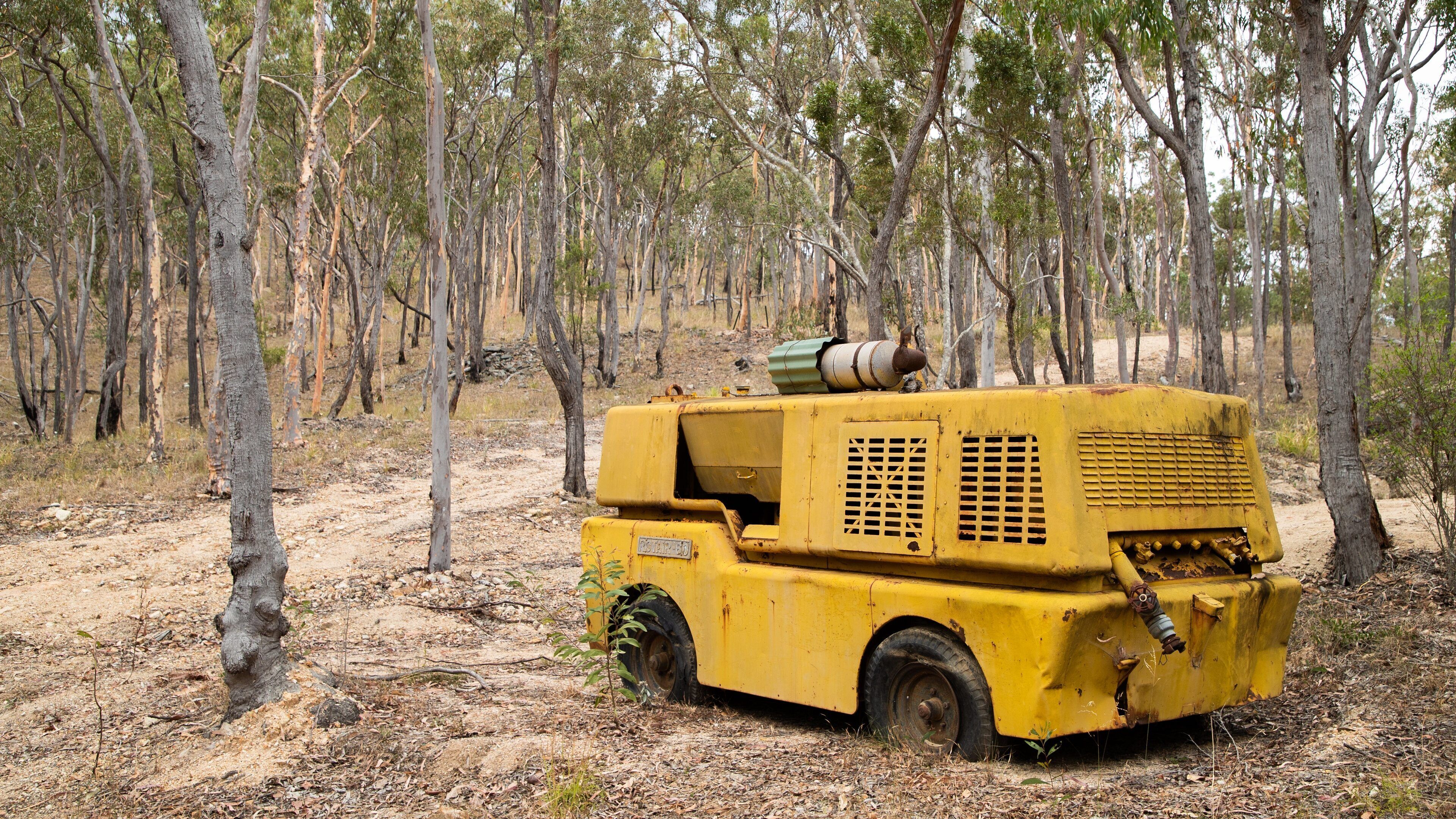 Um bulldozer amarelo numa floresta com árvores escassas e solo seco.