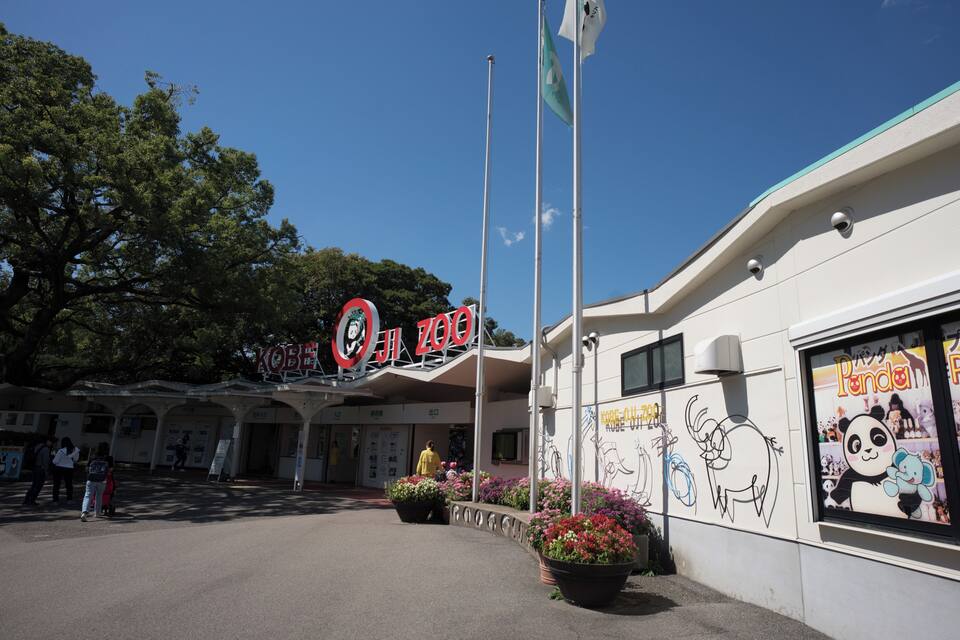 Entrada de um jardim zoológico com uma placa, bandeiras e um cartaz de panda.