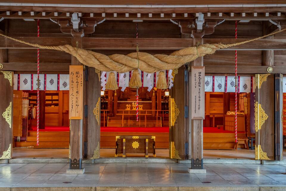 Um santuário japonês tradicional com pilares de madeira, um tapete vermelho e decorações penduradas.