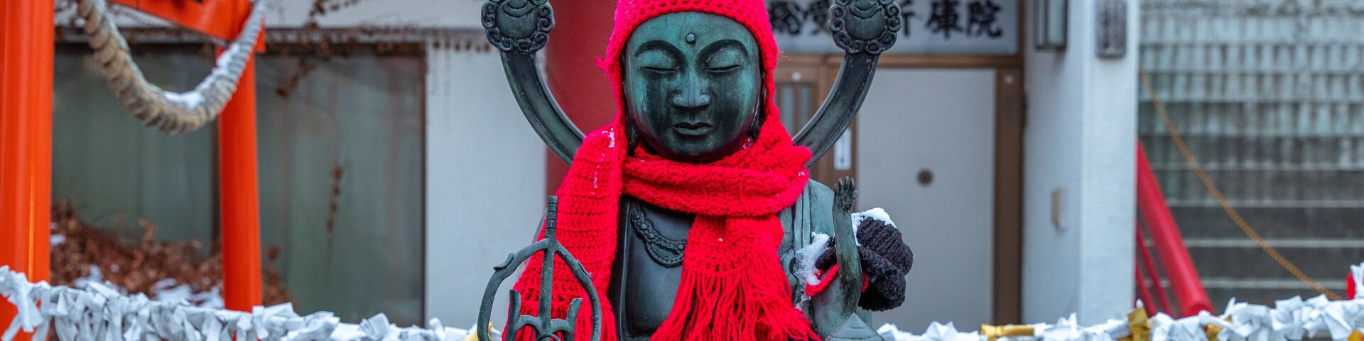 Uma estátua de uma figura com cachecol vermelho e um halo, rodeada por enfeites de papel branco.
