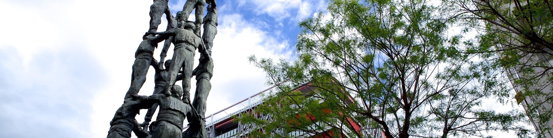 Grande estátua de bronze retrata soldados escalando uma estrutura, com um edifício e árvores ao fundo.