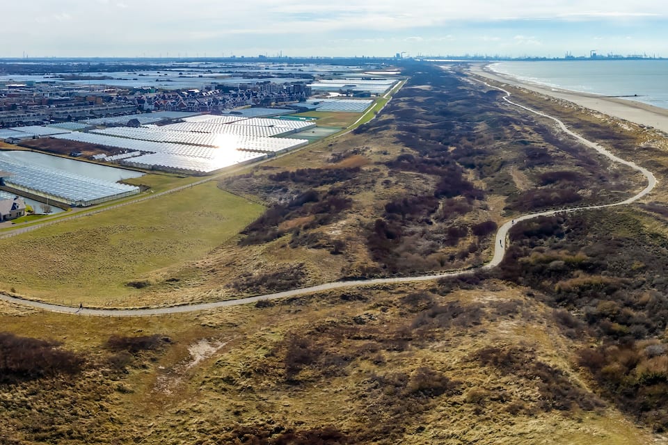 Vista aérea de uma área costeira com parques solares, uma estrada sinuosa e uma praia.