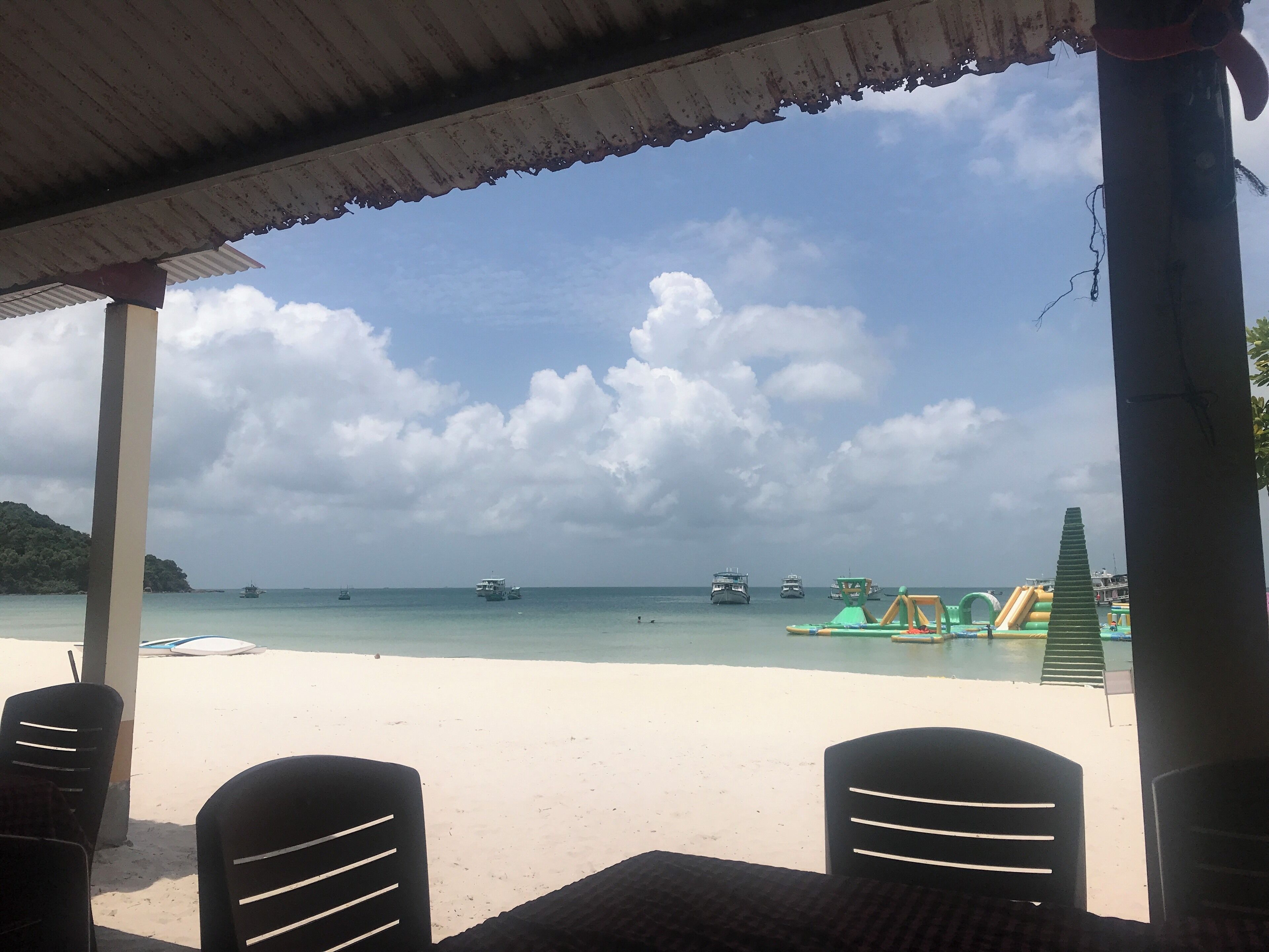 Uma praia com céu claro, vários barcos e um parquinho.