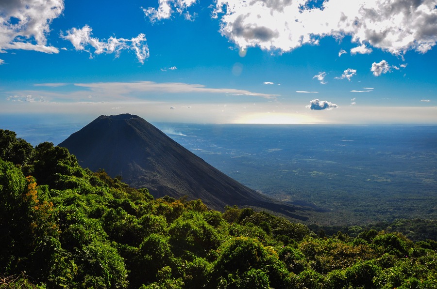 Montanha com uma floresta verdejante na base, sob um céu azul límpido com nuvens esparsas.