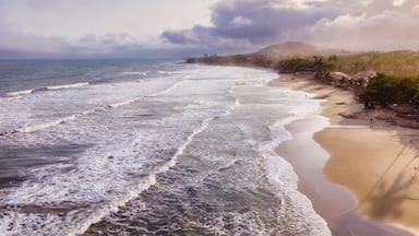 Uma praia com ondas, areal e uma montanha ao longe.