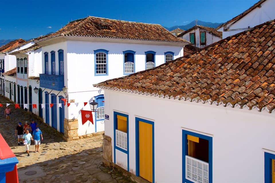 Uma rua de paralelepípedos flanqueada por edifícios brancos com detalhes em azul e amarelo, sob um céu azul claro.