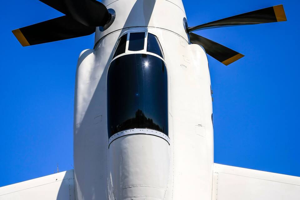 Uma aeronave grande com nariz vermelho e quatro hélices, montada sobre uma estrutura branca.