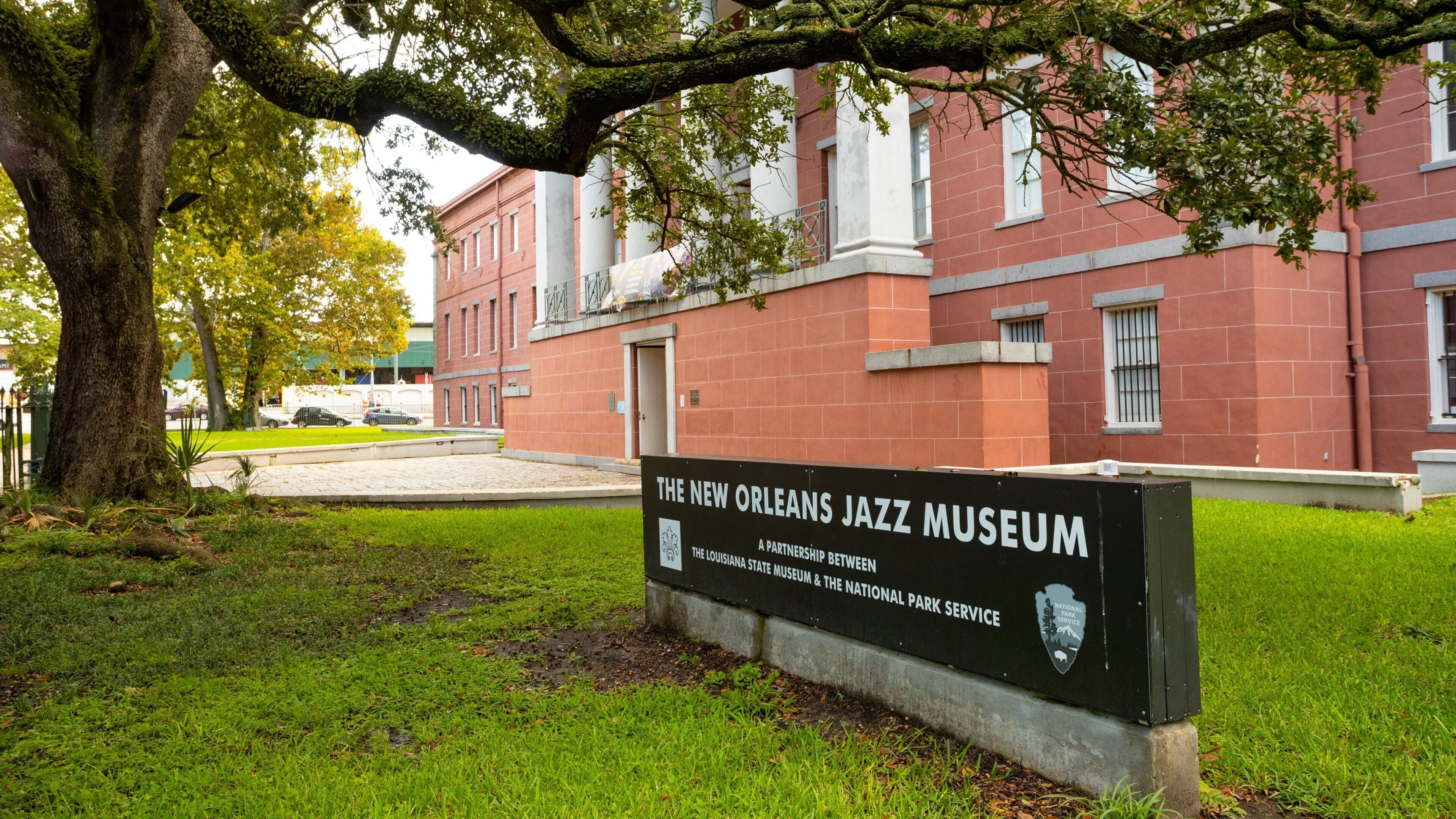 Placa do Museu de Jazz de Nova Orleans, rodeada por vegetação exuberante e uma grande árvore.