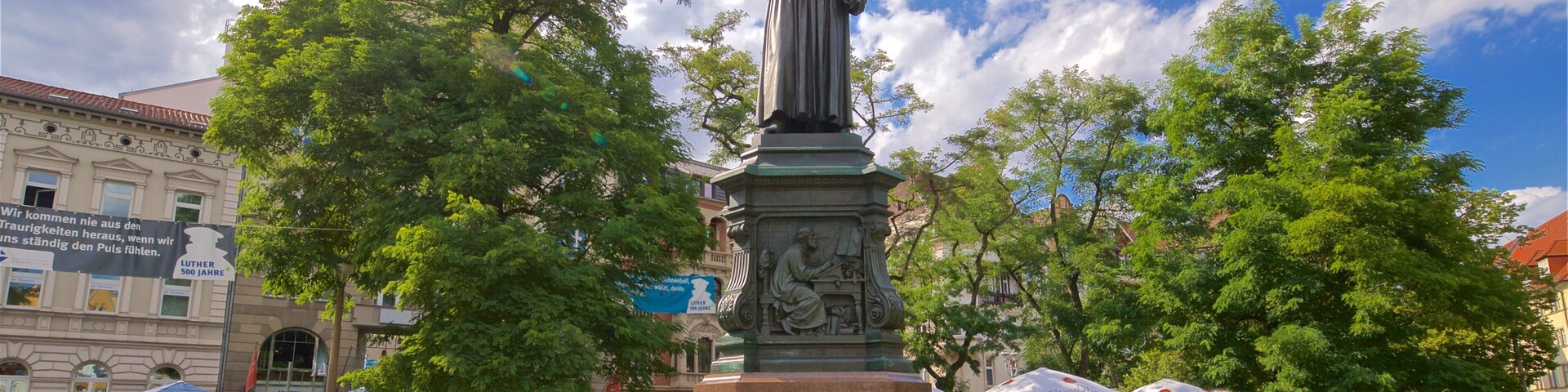 Uma estátua em um parque, com árvores e um edifício ao fundo.