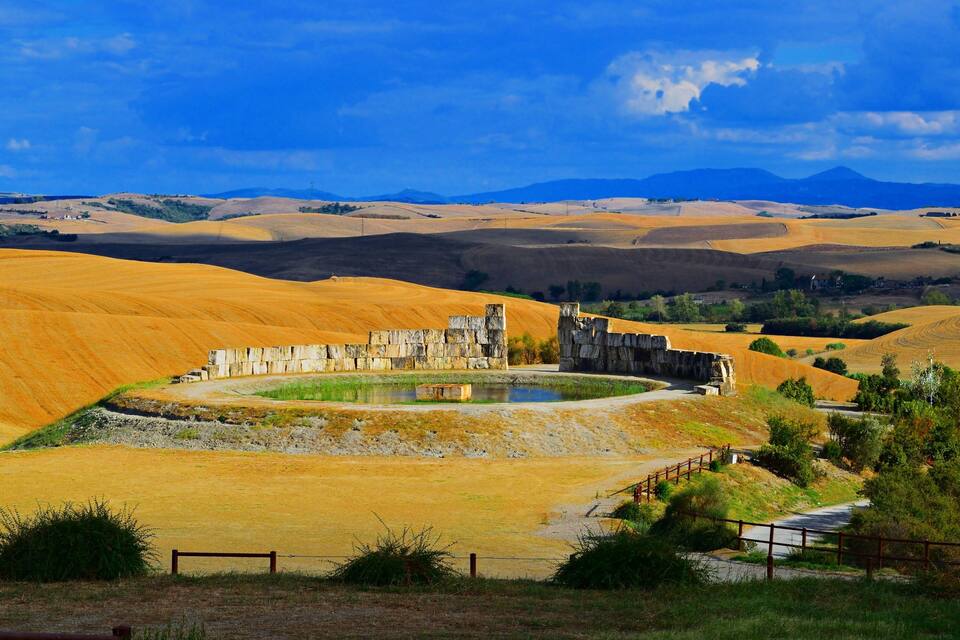 Uma construção de pedra histórica num vale com colinas ondulantes e céu claro.