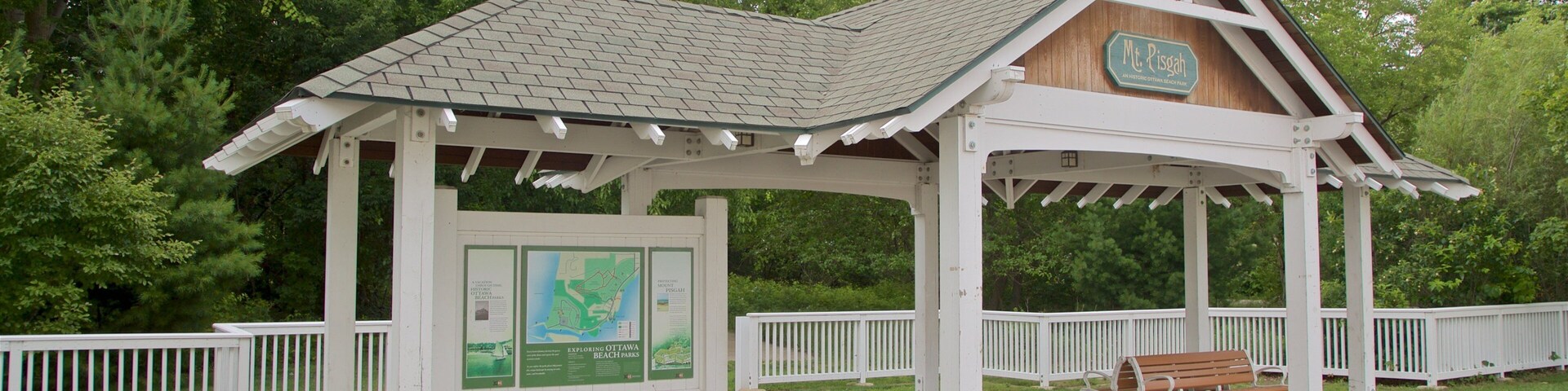 Um gazebo com uma placa que diz "Mt. Pisgah" em um parque com cerca branca e árvores verdes.