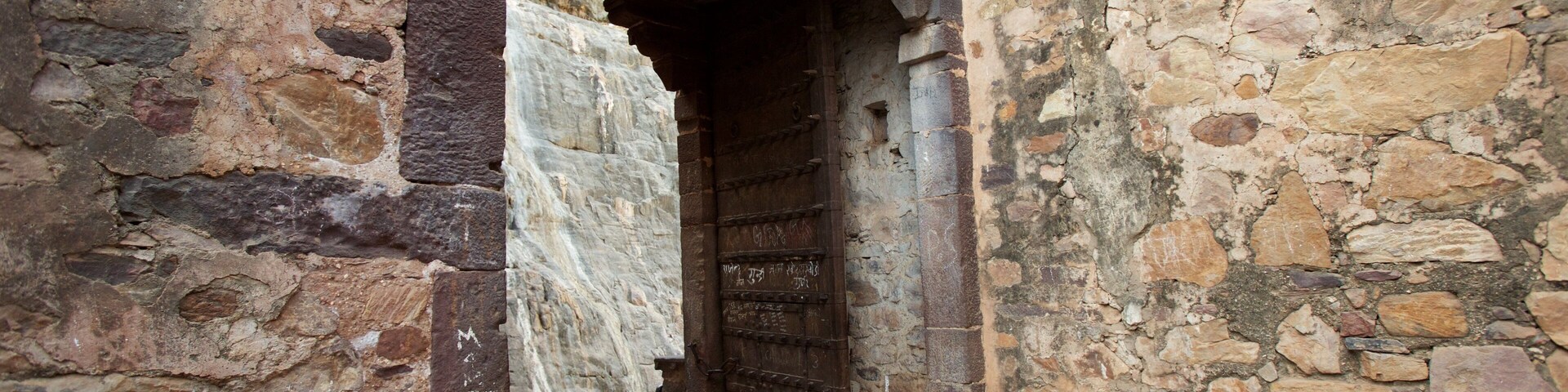 Um arco de pedra antiga que dá acesso a uma porta de madeira.