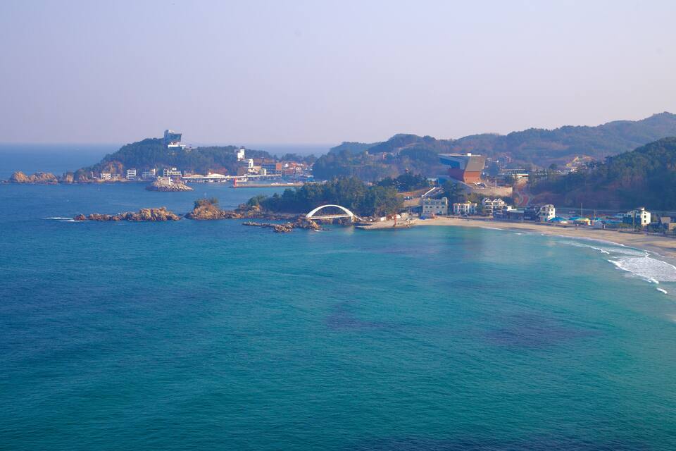 Uma vila costeira com uma ponte branca marcante, afloramentos rochosos e edifícios numa encosta.