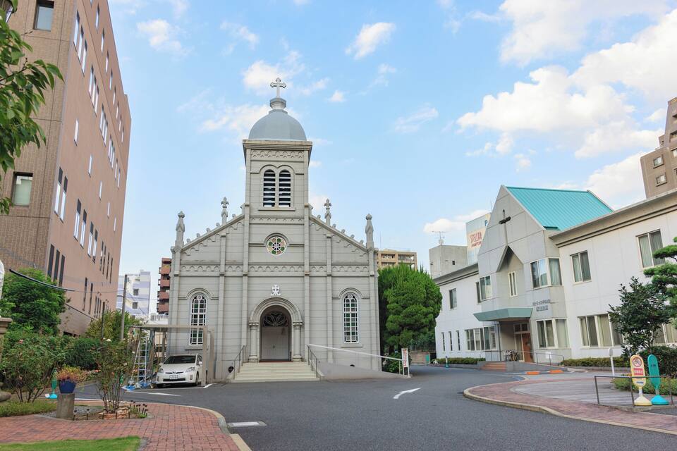 Igreja com um campanário, rodeada por edifícios modernos e um céu limpo.