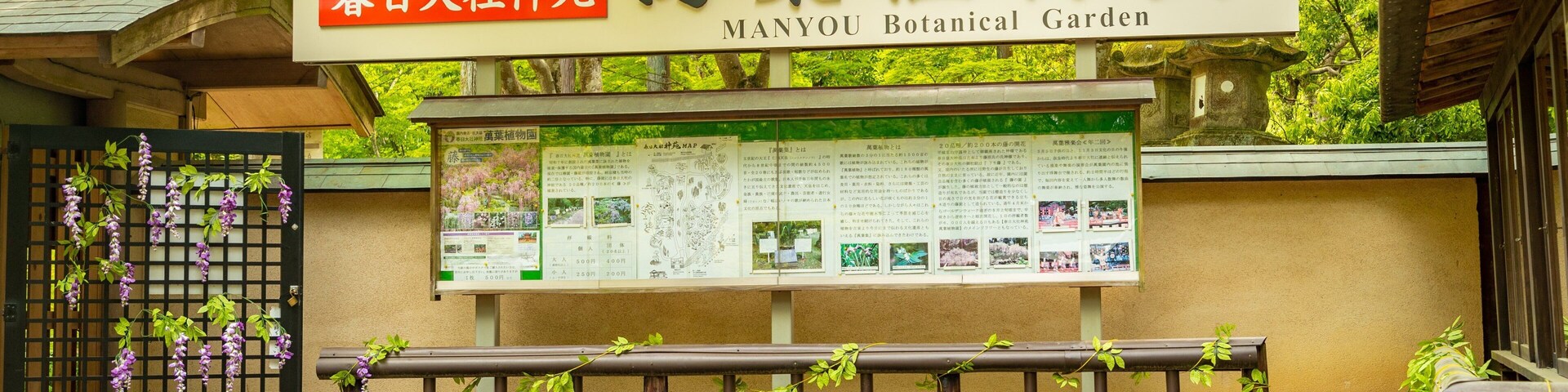 Entrada de um jardim botânico, com uma placa em vários idiomas e um mural de informações.