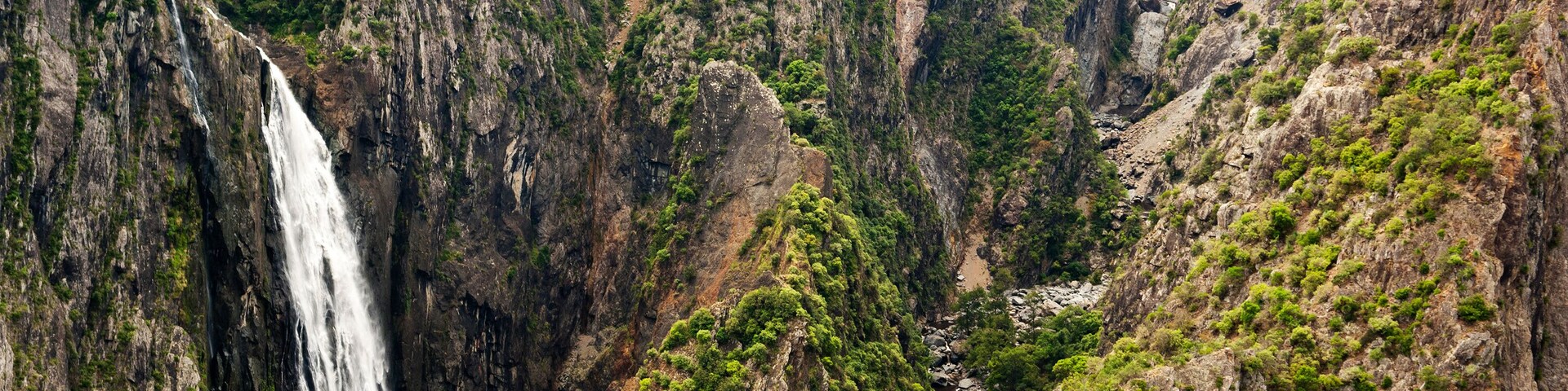 Uma cascata desce por um penhasco íngreme, cercada por vegetação densa.