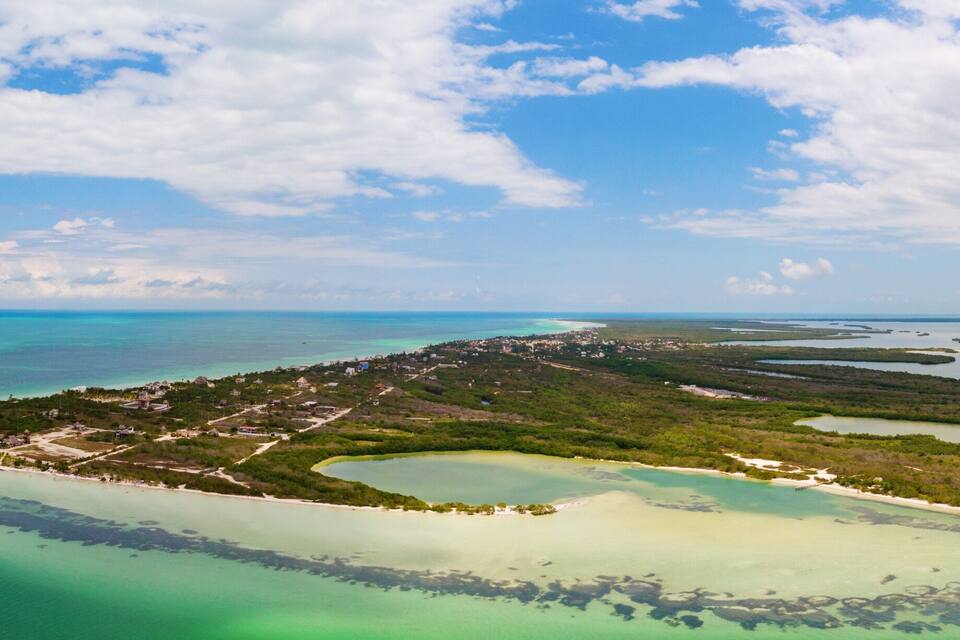 Vista aérea de uma ilha costeira com águas turquesa cristalinas, uma praia de areia e um pequeno povoado.