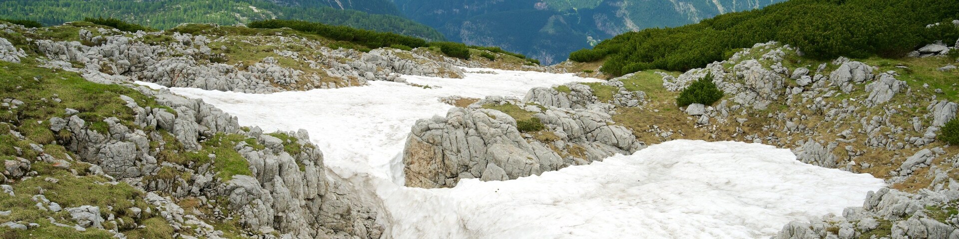 Uma geleira em uma paisagem montanhosa com terreno rochoso e cadeias de montanhas ao longe.