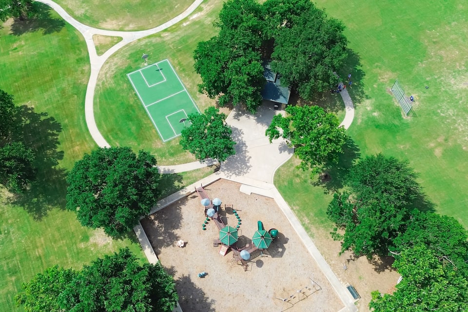 Vista aérea de um parque com quadra de tênis, parquinho e caminhos para pedestres.