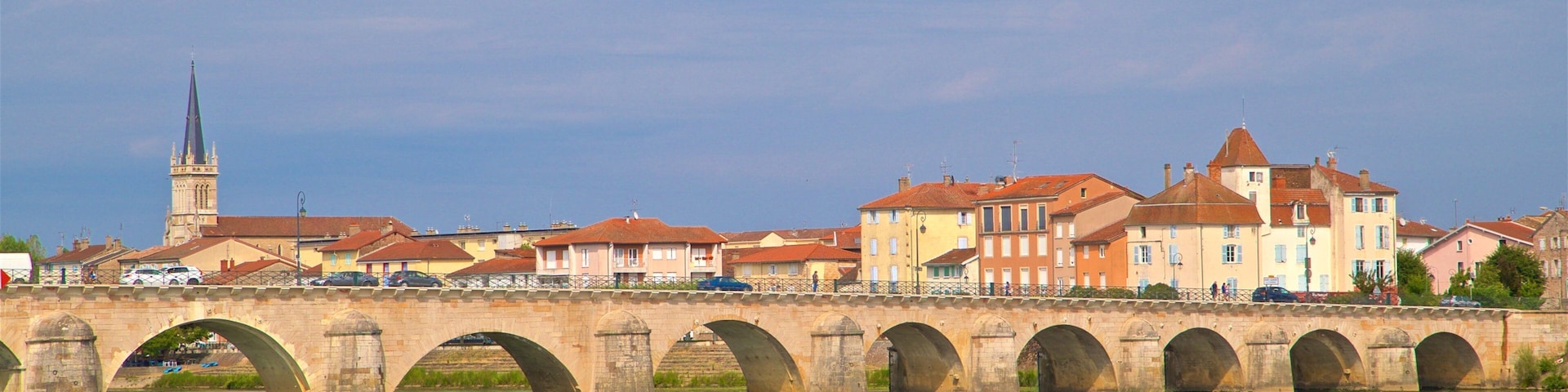 Uma ponte de pedra com várias arcos atravessando um rio, com edifícios e uma igreja ao fundo.